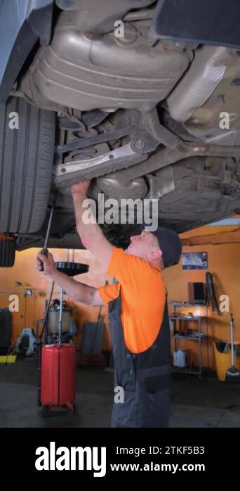 Vertical video of a young mechanic in a uniform working in a car repair ...