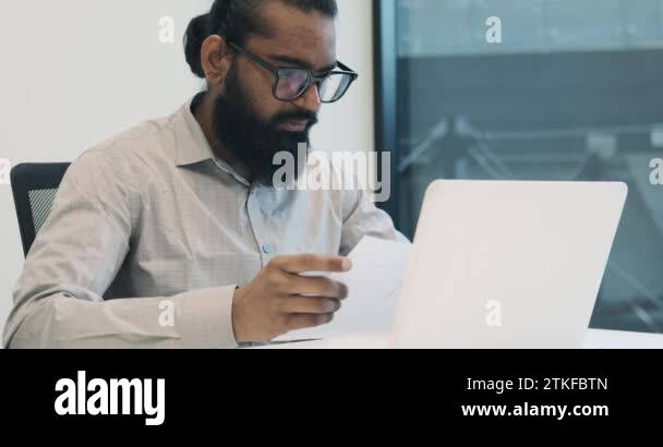 Seated at his desk in the office, an Indian businessman meticulously ...