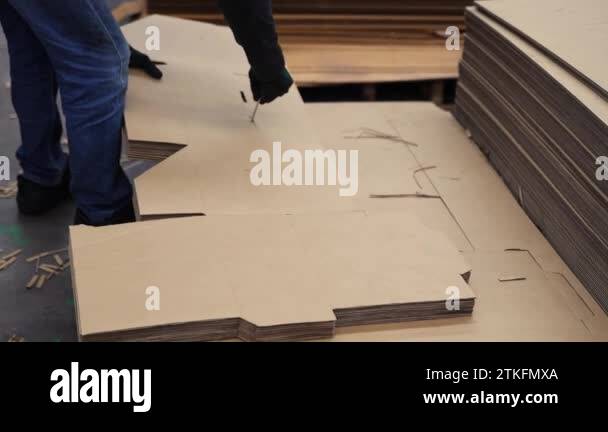 Male worker uses special tool to punch holes in stacked cardboard boxes ...