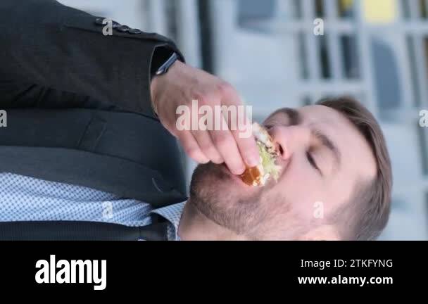 A young American office worker is having lunch outdoors, he is eating a ...