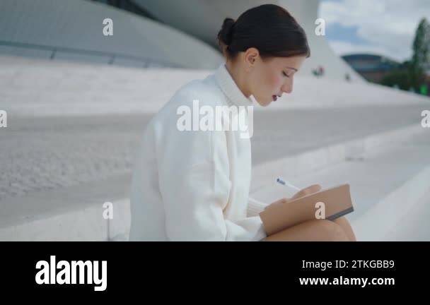 Attractive young girl student making notes in notebook sitting stairs ...