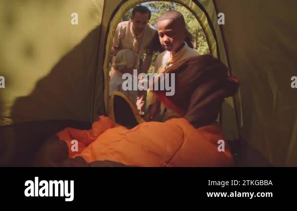 Little African American boy scout putting sleeping bag in tent while ...