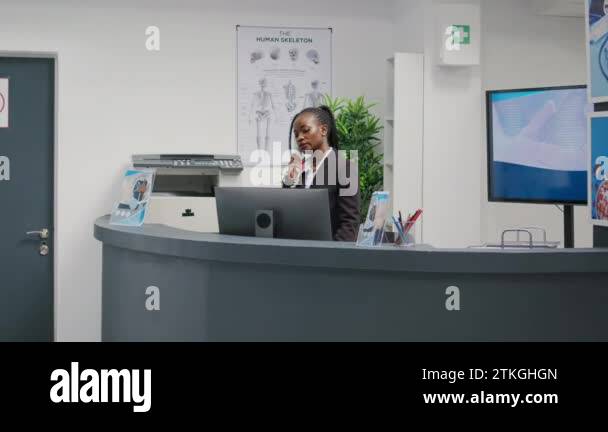 Young health center employee working at reception desk, answering ...
