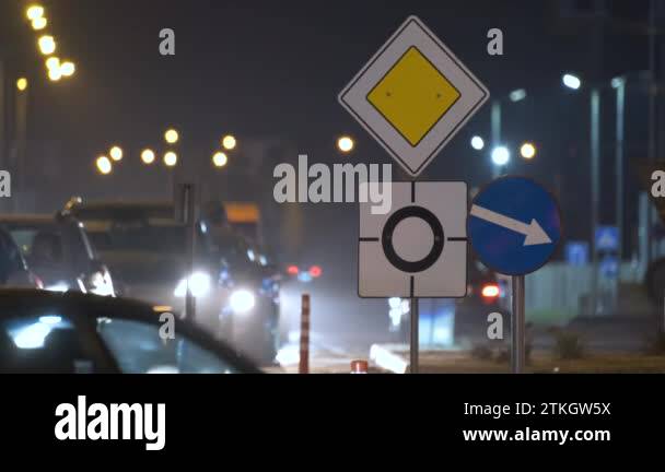 Roundabout road signs with blurred cars on city street traffic at night ...