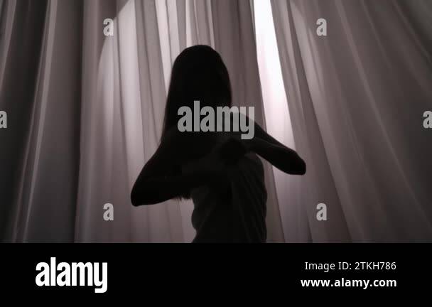Medium slow motion video of a young womans silhouette just out of the shower, taking a towel off ...