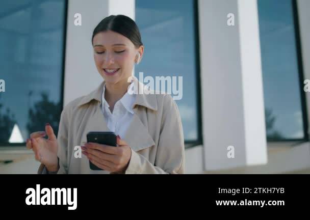 Smiling young woman saying goodbye in phone camera standing city street ...