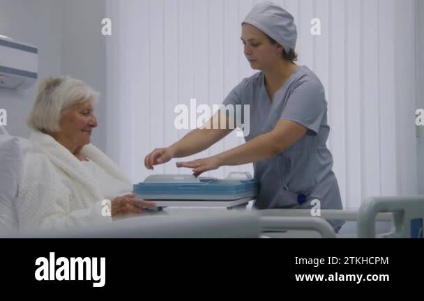 Nurse opens big lunch box with meal to female old patient. Elderly ...