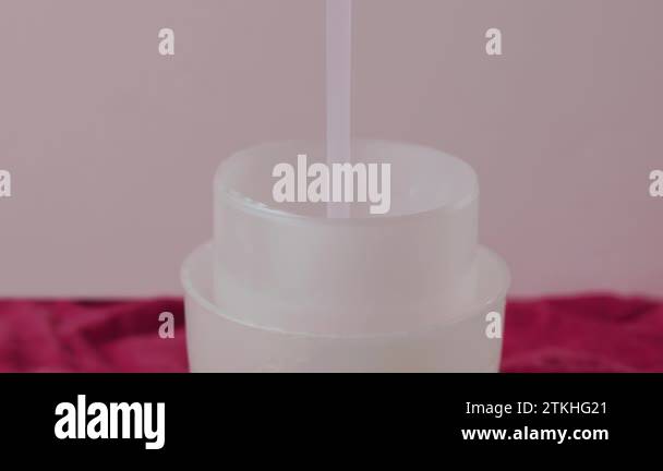 Stream of pink liquid laundry detergent poured into plastic measuring ...