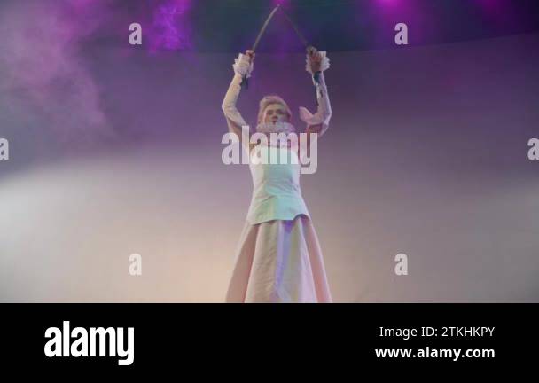 Actress in white elegant retro-style dress raising sword imitating ...