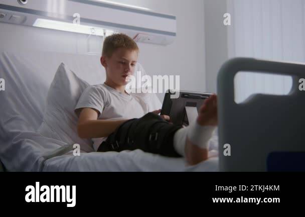 Young boy with bandaged leg lies on bed and talks with parents using ...