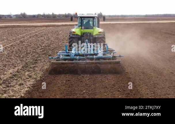 Tractor with harrow system plowing ground on cultivated farm field ...