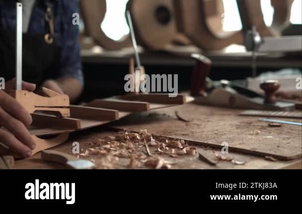 A skilled luthier is hard at work sanding the body of an acoustic ...