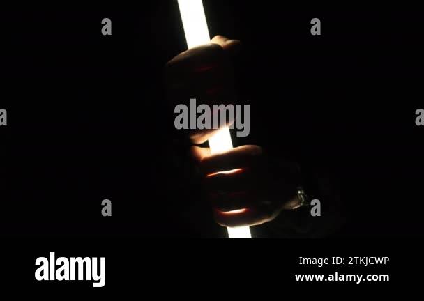 Mens hands hold a light sword against a black background. Male fingers ...