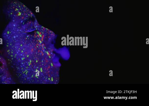 A beautiful young girl with makeup from ultraviolet paints smokes ...