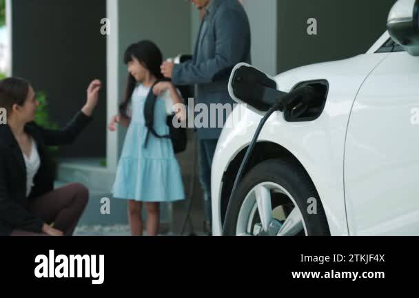 Progressive parents with electric vehicle and home charging station. Happy family with daughter ...