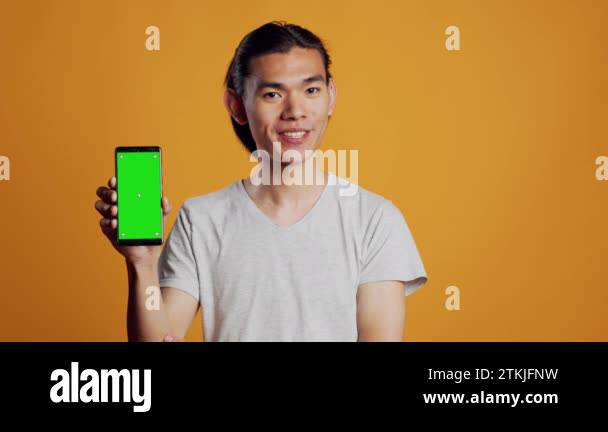 Asian male model showing smartphone with greenscreen on camera, looking ...