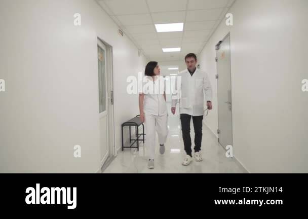 Two doctors man and woman, walk quickly down hospital corridor and ...