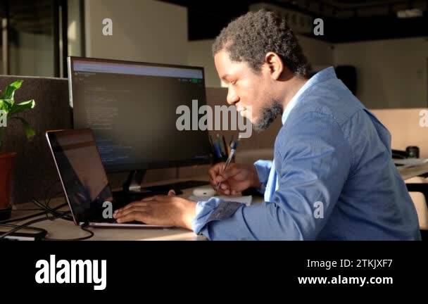 Black Man Writing Lines of Code On Desktop PC With Two Monitors and a ...