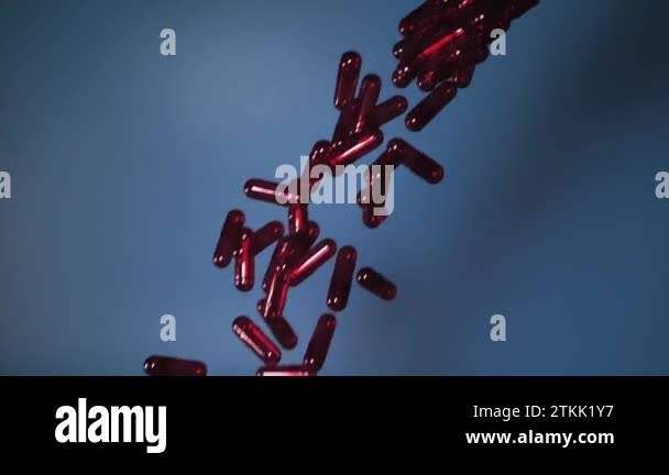 Red medicine capsules falling on a blue background. A group of ...