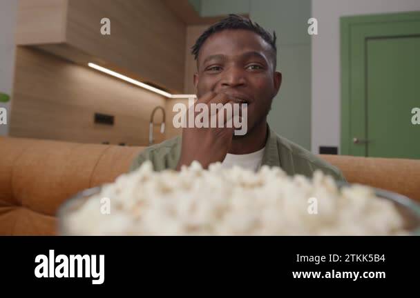 Black Man Eating Popcorn Looking at Camera. 20s African American male eating snacks. Close up ...