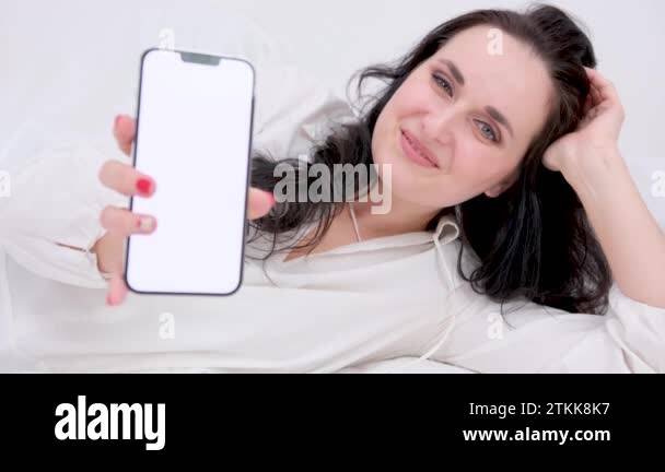 beautiful brunette holds phone with white screen close-up smiles ...