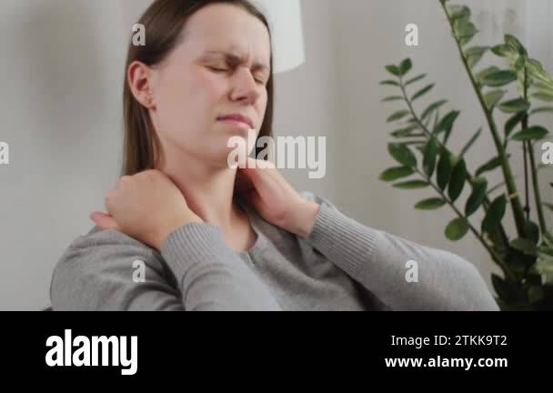 Unhappy young female sitting on couch touch neck suffer from painful ...