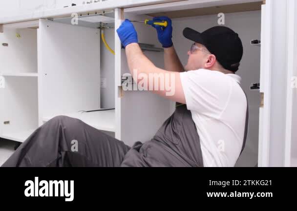 A qualified craftsman in special clothes installs the doors of a white ...