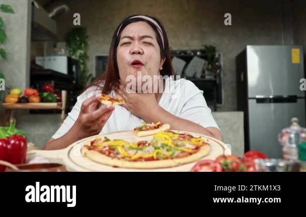 Obese Asian woman sits and eats her favorite glutton snack food pizza ...