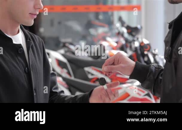 Close up of salesman giving motorcycle key to the client. Buyer dressed ...