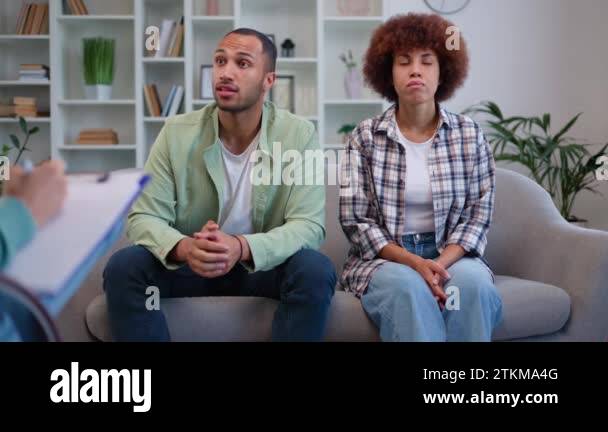 Multicultural married couple visiting psychologist to solve family issues. Young man sharing own ...