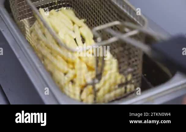 Male hand of cook shaking a lattice with french fries being prepared in ...