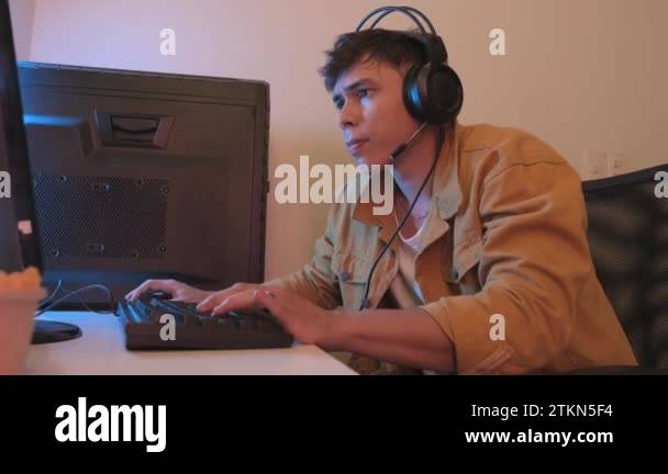 Gen z boy in headphones with microphone using keyboard while playing ...