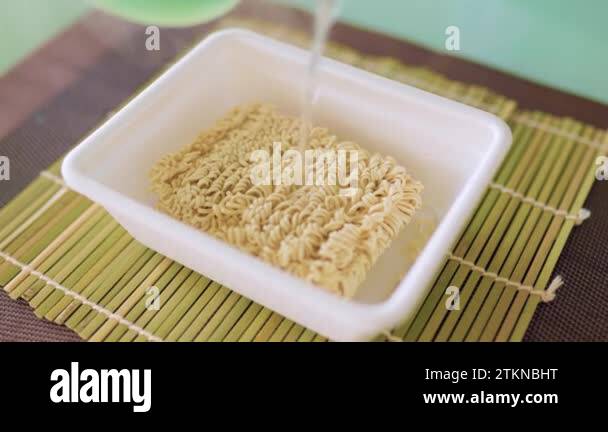 preparing instant noodles, with steam rising from the hot water as they ...