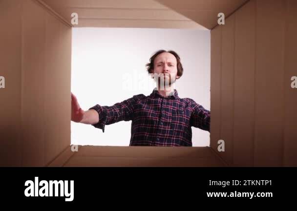 Doubting face. Young man unpacking, opening cardboard box and ...