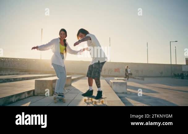 Happy pair riding skate boards at sunny stadium. Active curly guy ...