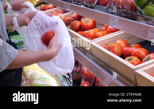 A woman in a store selects ripe tomatoes for her family to prepare ...