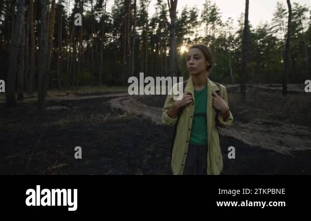 sad woman hiker with backpack in woods after forest fire. charred earth ...