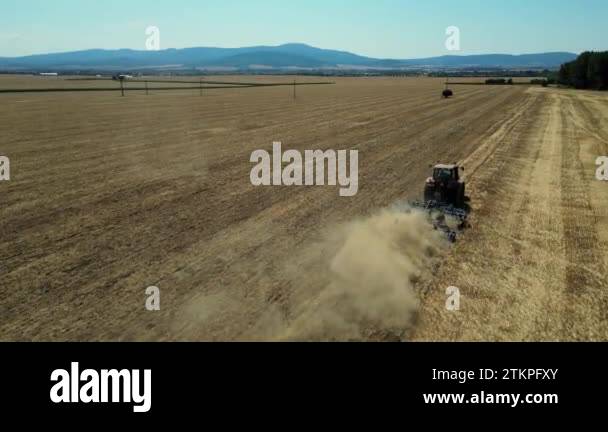Harrow system plowing ground on cultivated farm field, pillar of dust ...