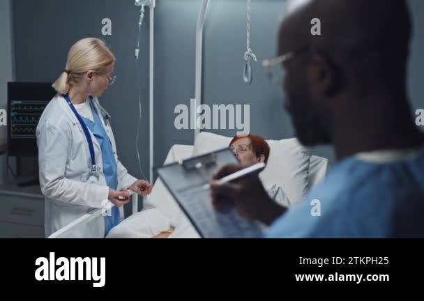 Over-shoulder of blurred Black male nurse taking notes of blond mature ...