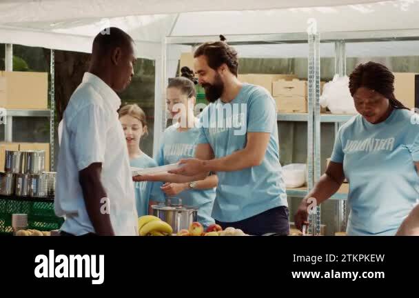 At community center young and pleasant group of volunteers serving warm food and helping the ...