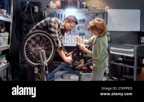 Beautiful caring skillful dad teaching cute little boy to fix bike in authentic workshop with ...