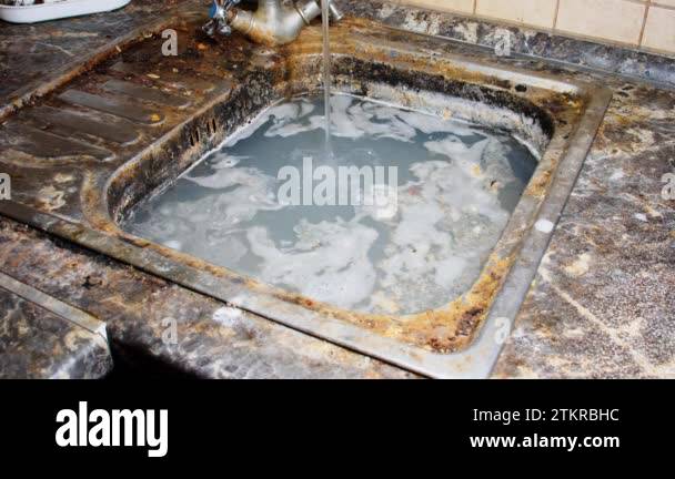 Tap water flows into a dirty kitchen sink. Dirty soapy water for ...