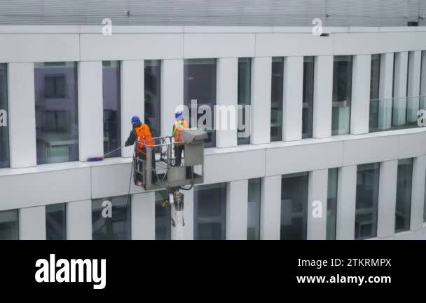Two workers wearing safety harness wipe walls, panels and windows of ...