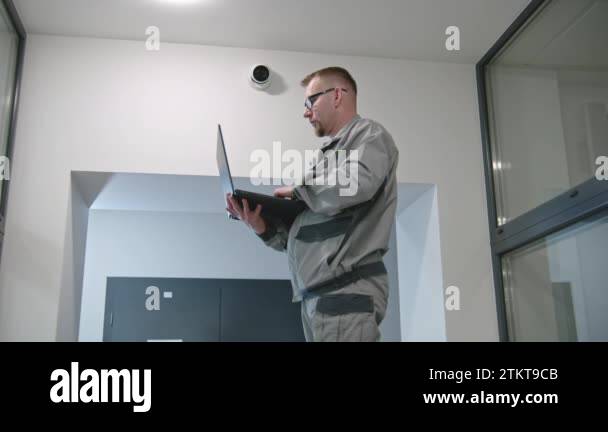 Installer in uniform sets up security camera in office room using ...