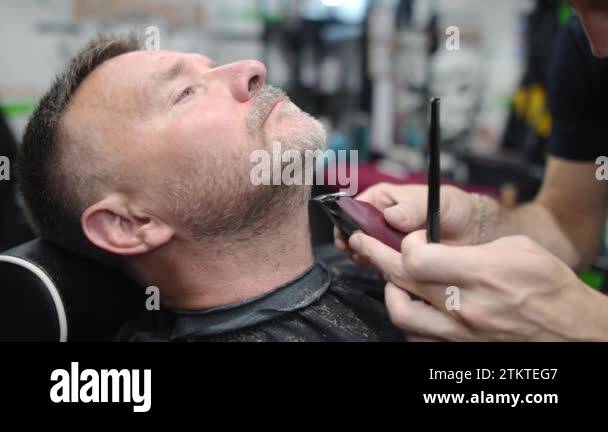 Barber master is shaving of handsome mature bearded man in salon. Hair ...