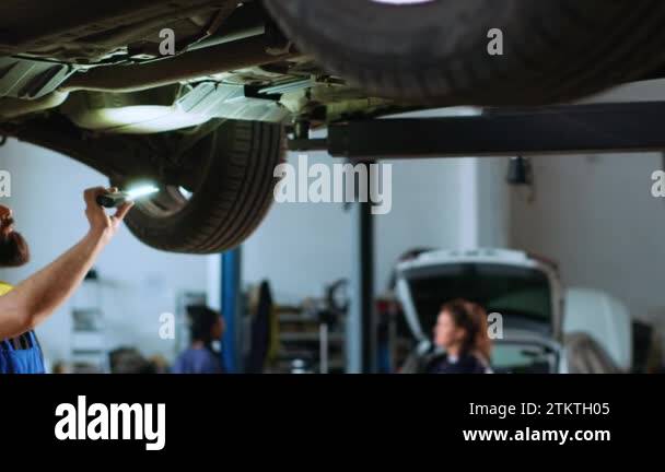 Certified repairman underneath vehicle on overhead lift in garage ...