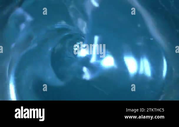 The surface of clear blue water swirls into a whirlpool and a funnel is ...