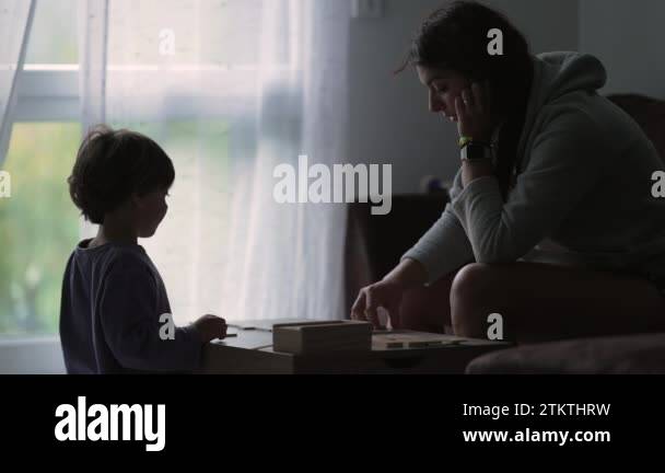 Candid mother and child playing board game at home in silhouette by ...