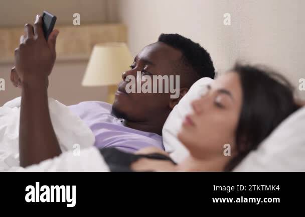 Close-up portrait of interracial couple in bed. African man using ...