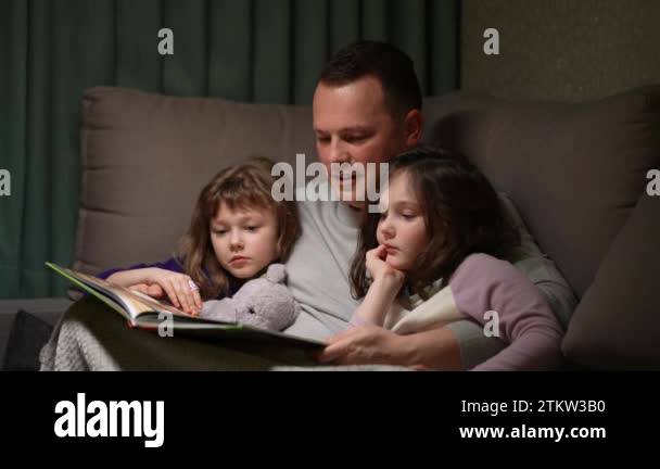 Father reads an interesting book to children at home. A loving father ...